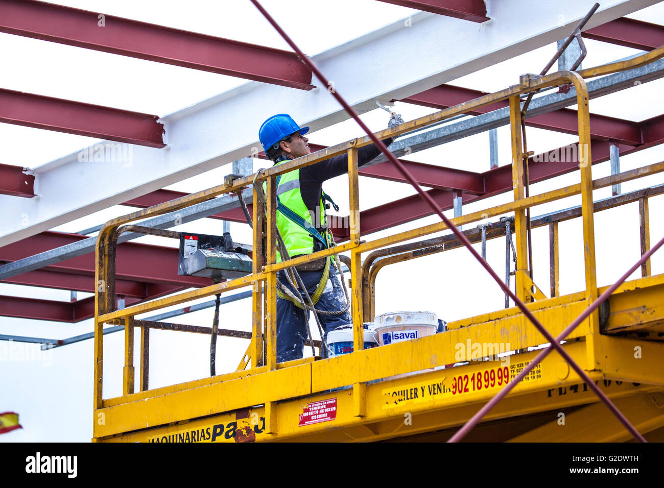 male painter working on a yellow lifting work platform beside a dock in ...