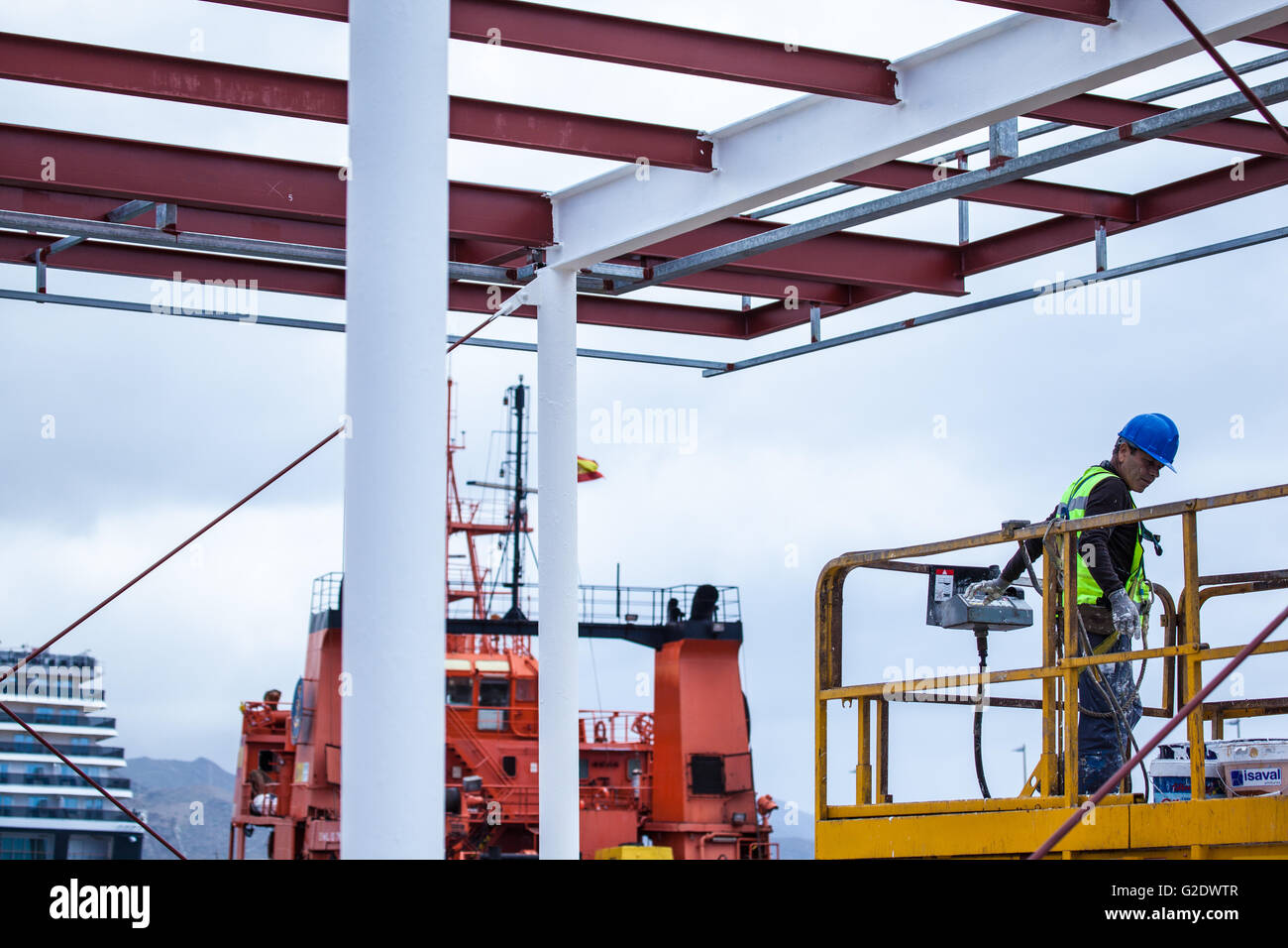 male painter working on a yellow lifting work platform beside a dock in ...