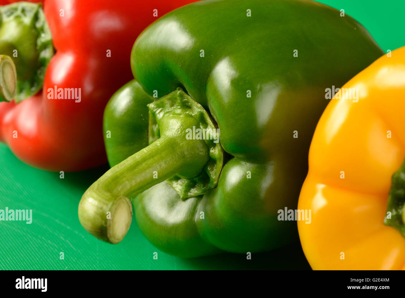 Red, green and yellow bell peppers on green chopping board - the ...