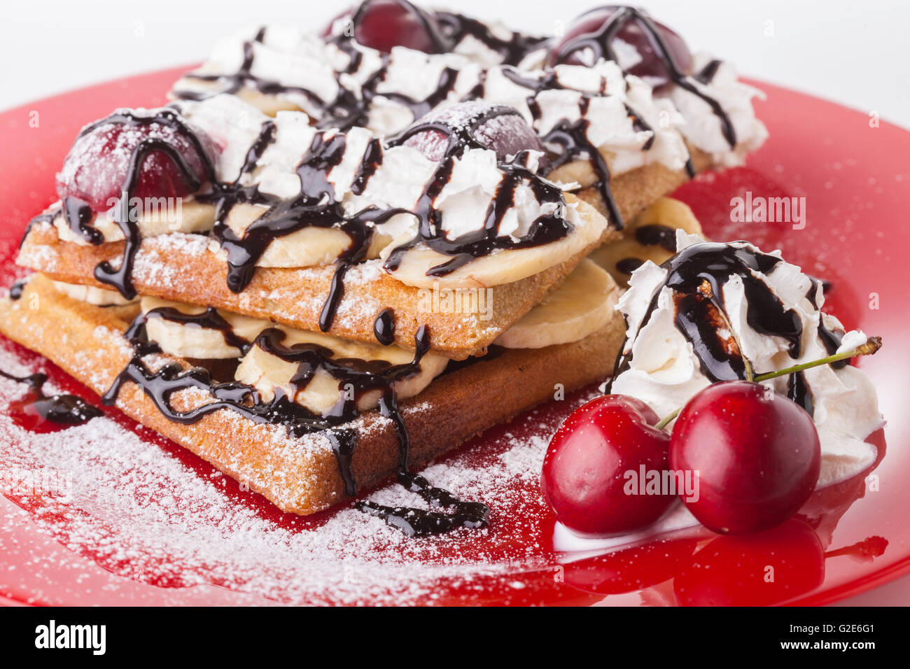 Belgian waffle with chocolate syrup whipped cream and red cherry on red ...