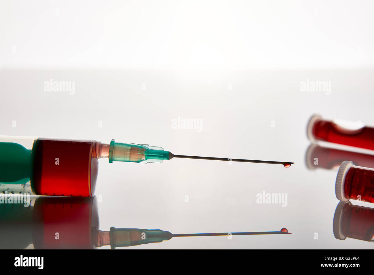 Syringe and vials with blood sampling over white glass table ...