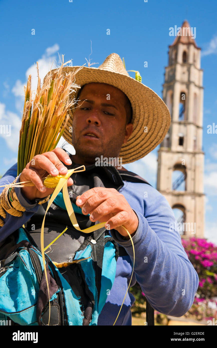 Vertical portrait of a man making a grasshopper from a sugar cane leaf ...