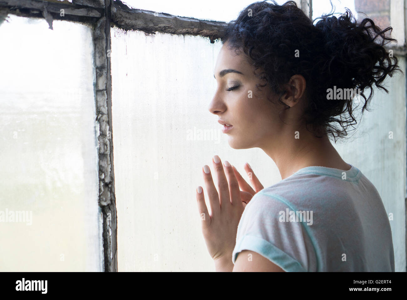 Sad young woman leaning against the window Stock Photo - Alamy