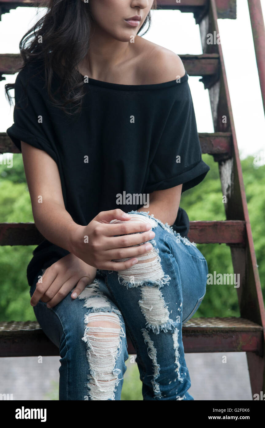Young woman in ripped jeans sat on steps outdoors Stock Photo - Alamy