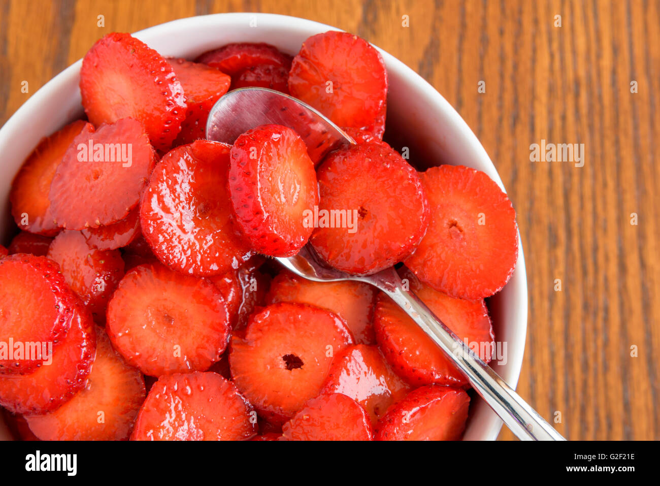 Close up of a bowl of sliced strawberries and a spoon on a wood table ...