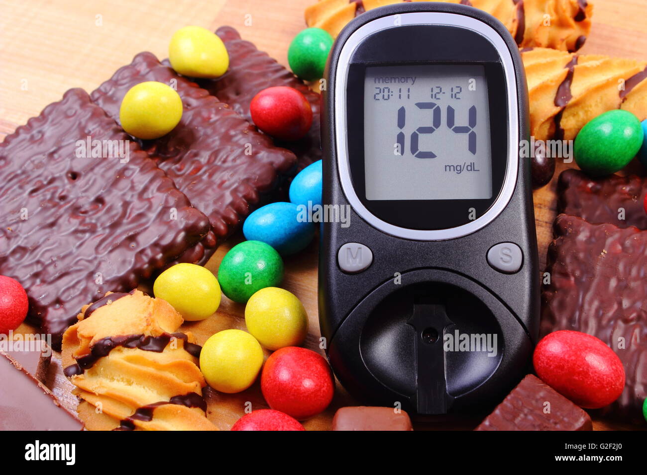 Glucose meter with heap of candies and cookies on wooden table, too ...