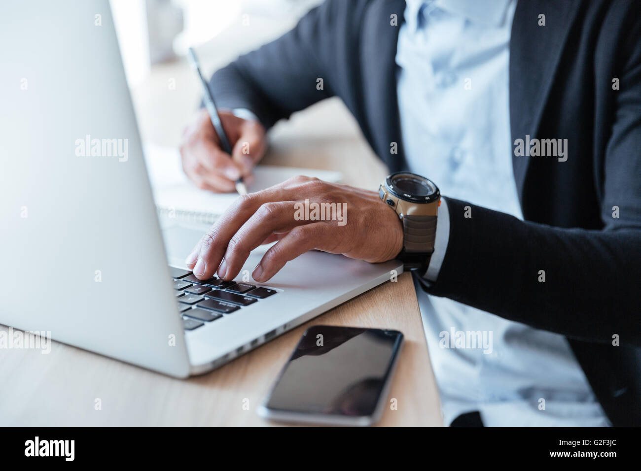 Close-up portrait of multitasking mans hands using laptop and writing ...