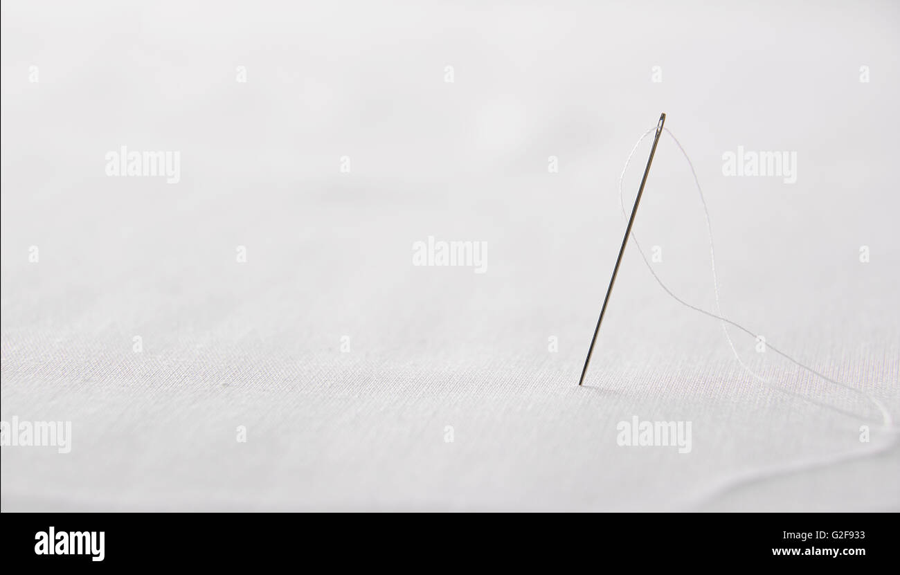 Needle with thread on white fabric background. Horizontal composition ...