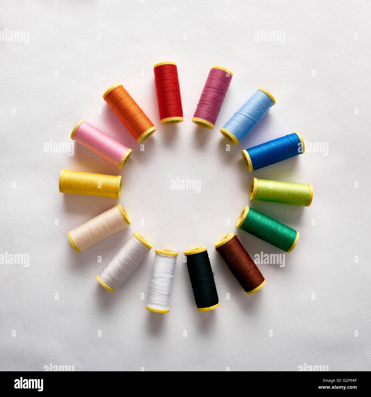 Spools of thread in circle on white cloth. Square composition. Top view ...