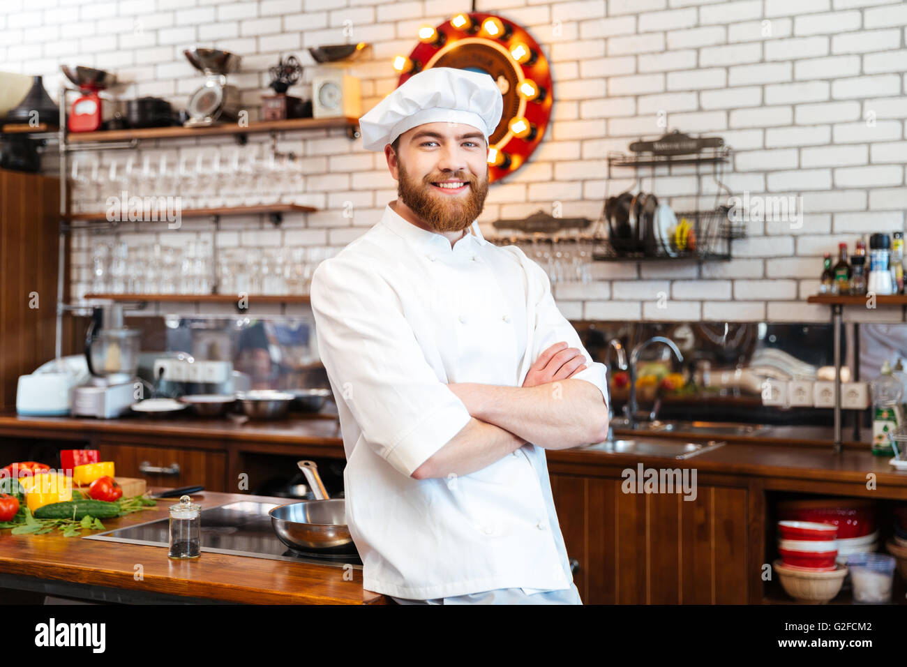 Smiling attractive chef cook with beard standing with hands folded on ...
