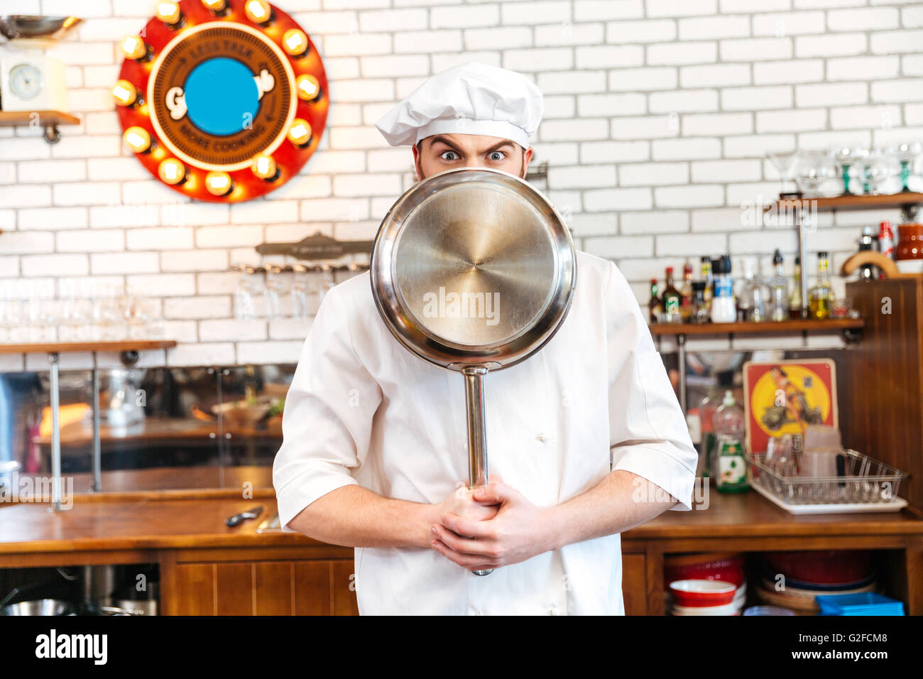 Funny young chef cook covered his face with frying pan on the kitchen ...