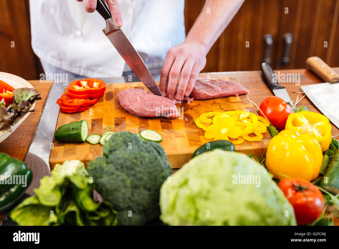 Hands of chef cook cutting and preparing meat with fresh vegetables on ...