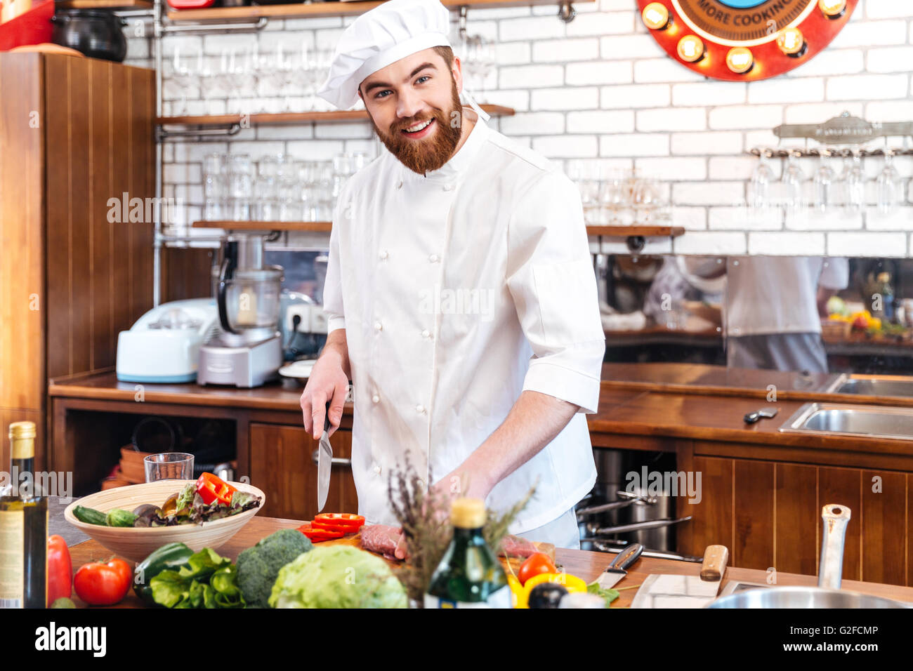 Cheerful handsome young chef cook cutting meat and making vegetable ...