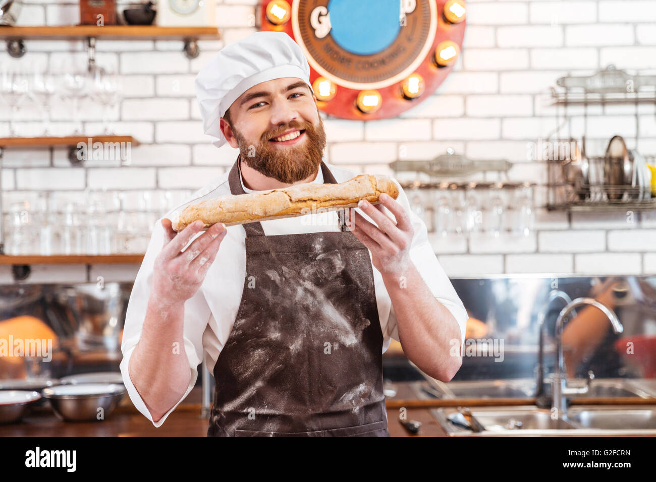 Cheerful attractive baker standing and showing loaf of bread on the ...