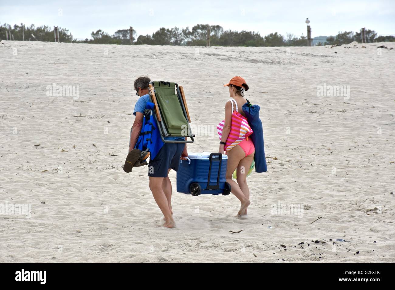 A couple carrying a cooler and beach chairs off the beach after a fun ...