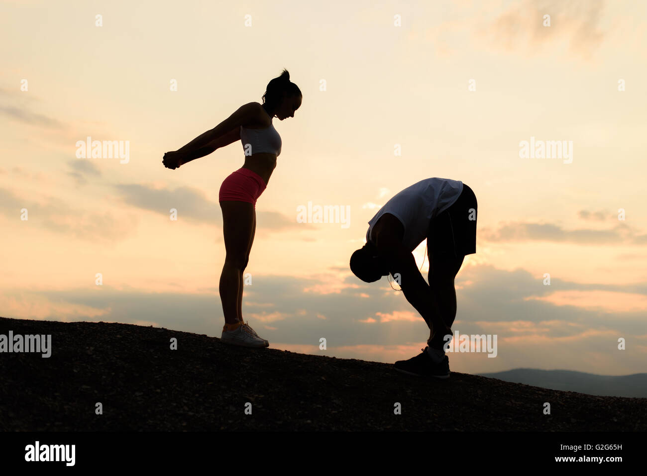 Silhouettes of fit mixed race couple stretching together on the rocky ...