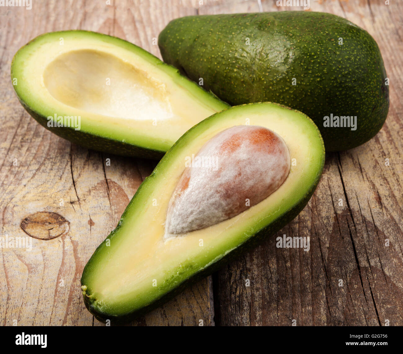 Two avocado one cut in half on old brown wood Stock Photo - Alamy