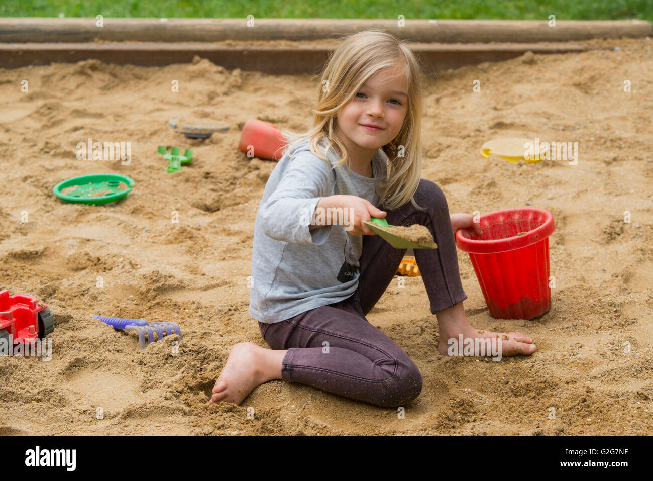 Little blond girl is playing in sandbox with plastic toy tools Stock ...
