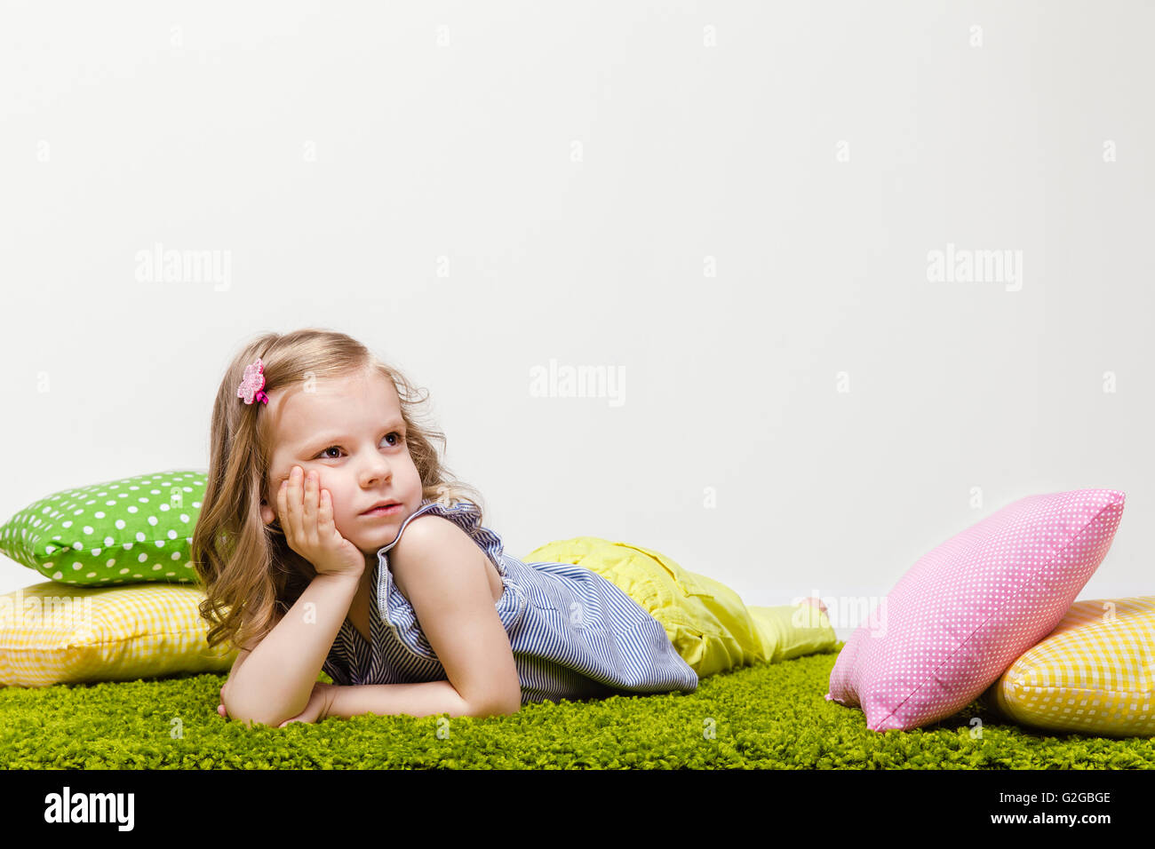 Girl lies on a green rug with pillows and looks sideways Stock Photo ...