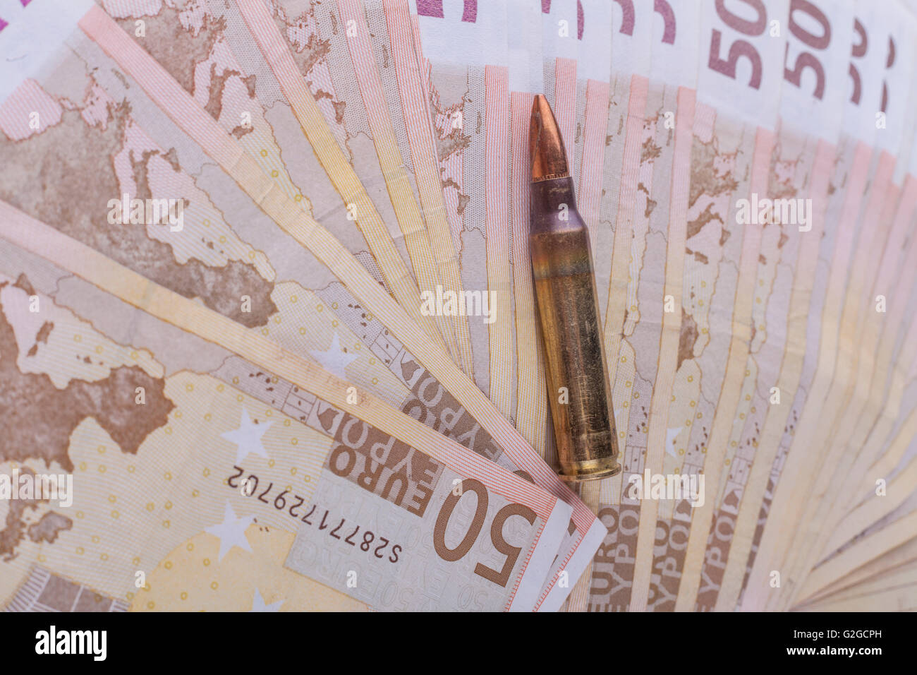 Single rifle bullet closeup with a pile of euro banknotes in the ...