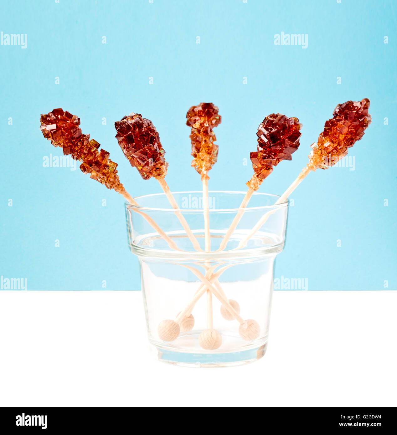 Five brown sugar stirrers in a glass on a white table with light blue ...