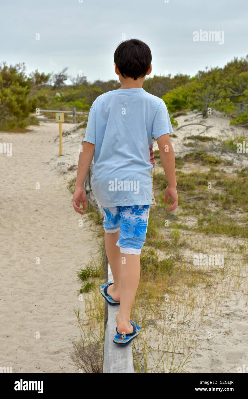 A young boy trying to balance as he walks across the top of a wood ...