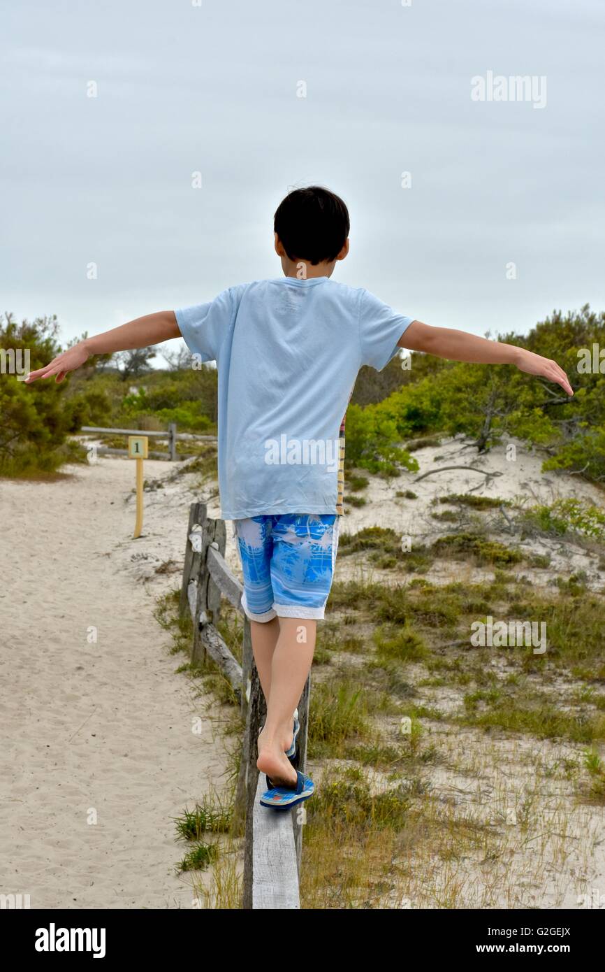 A young boy trying to balance as he walks across the top of a wood ...