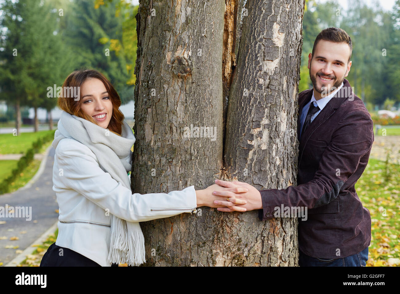 Couple peeking around opposite sides of tree Stock Photo - Alamy