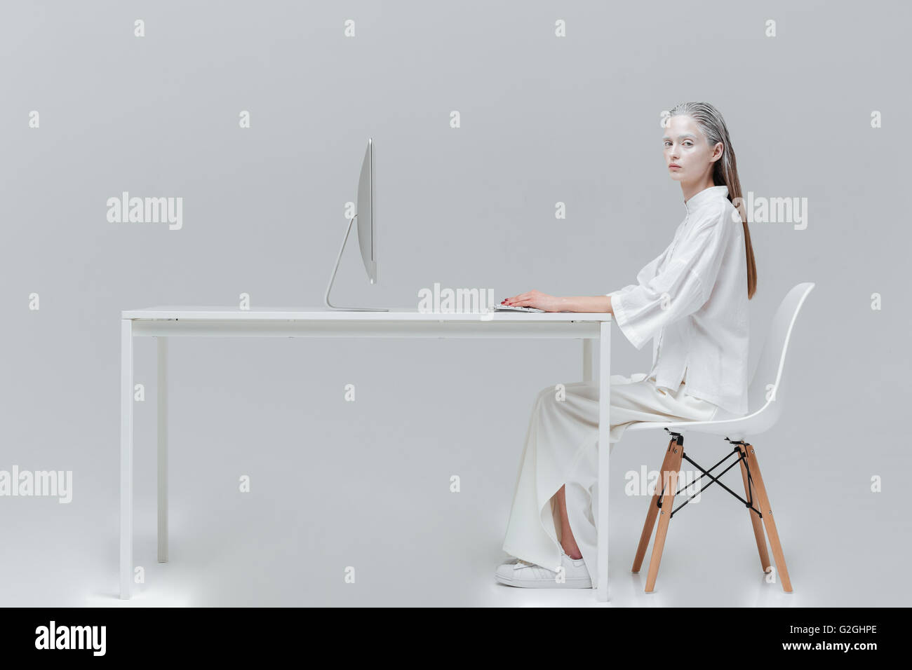 Fashion beautiful girl sitting at the desk with computer, pc over gray ...