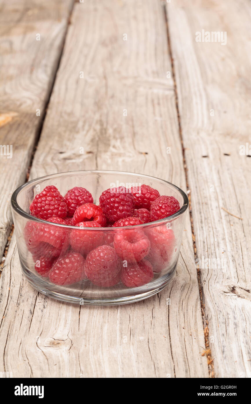 Clear glass bowl of ripe raspberries on a rustic farm picnic table in ...