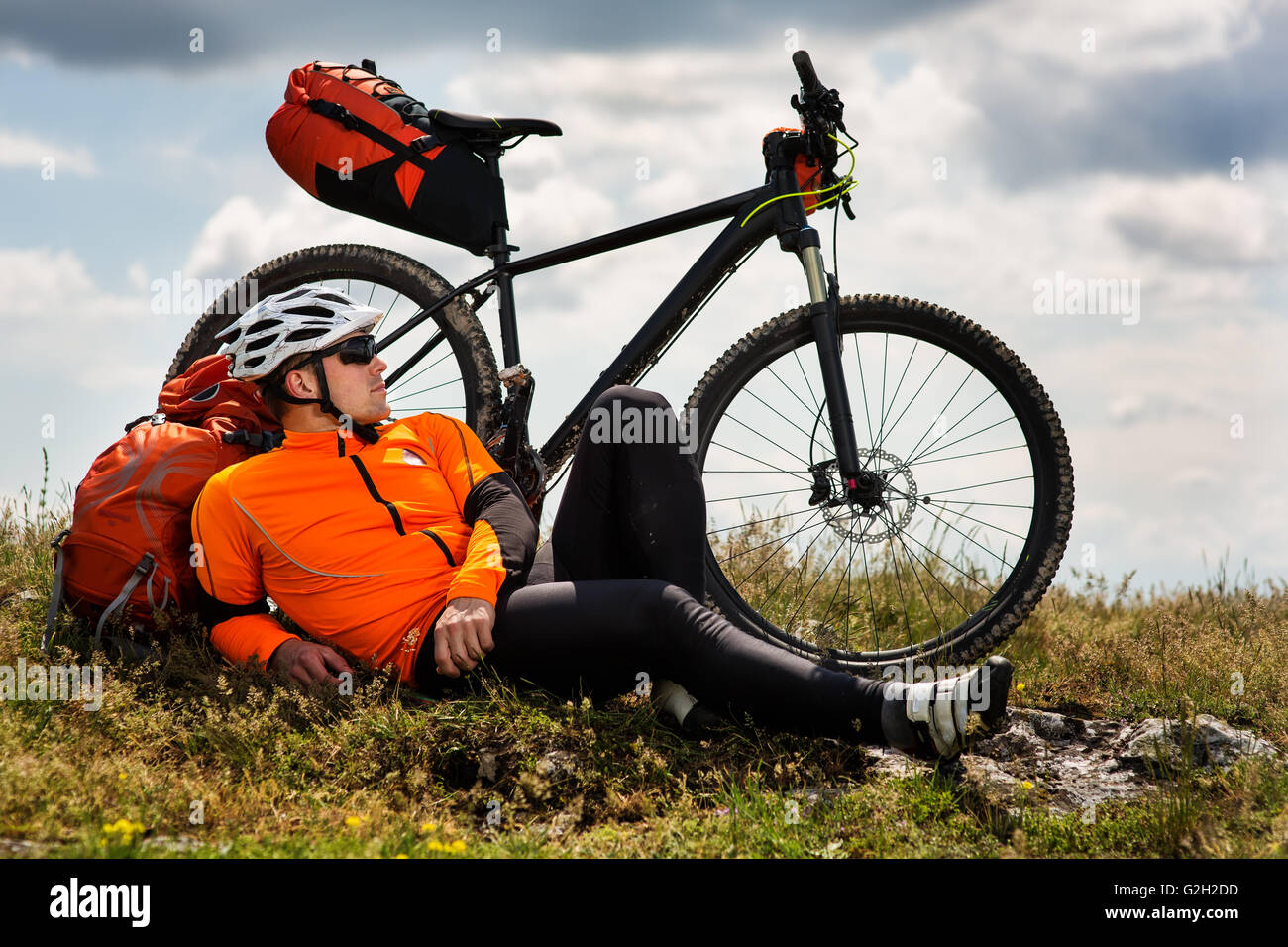 Young man sitting near the cycle on a green meadow Stock Photo - Alamy