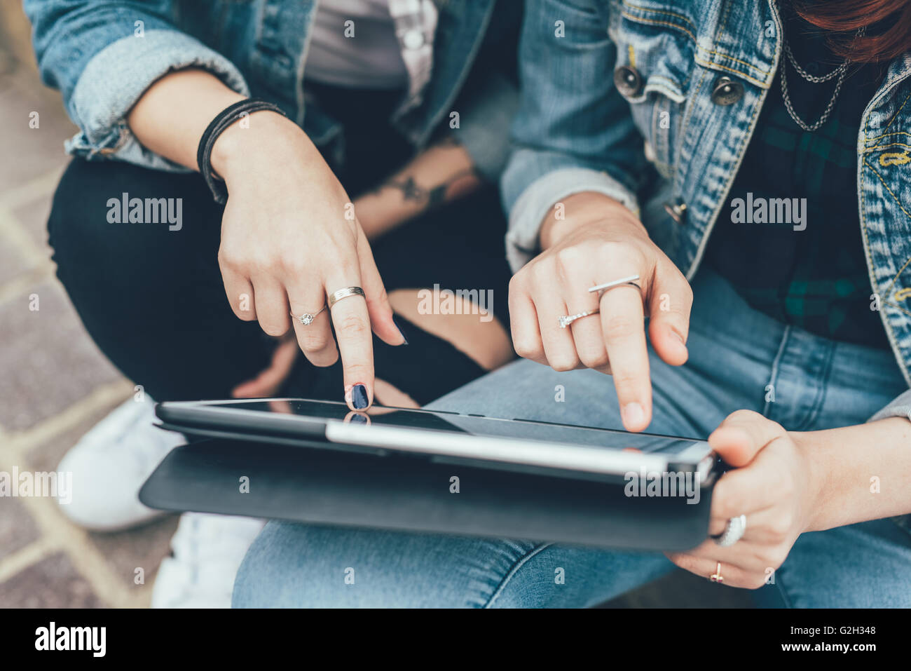 Close up on the hands of two young women tapping the screen of tablet ...