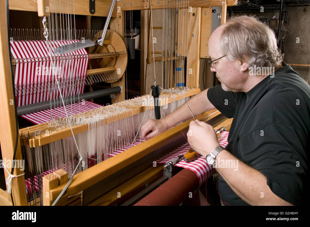 Man fixing broken thread on loom while weaving checkered dish towels on ...