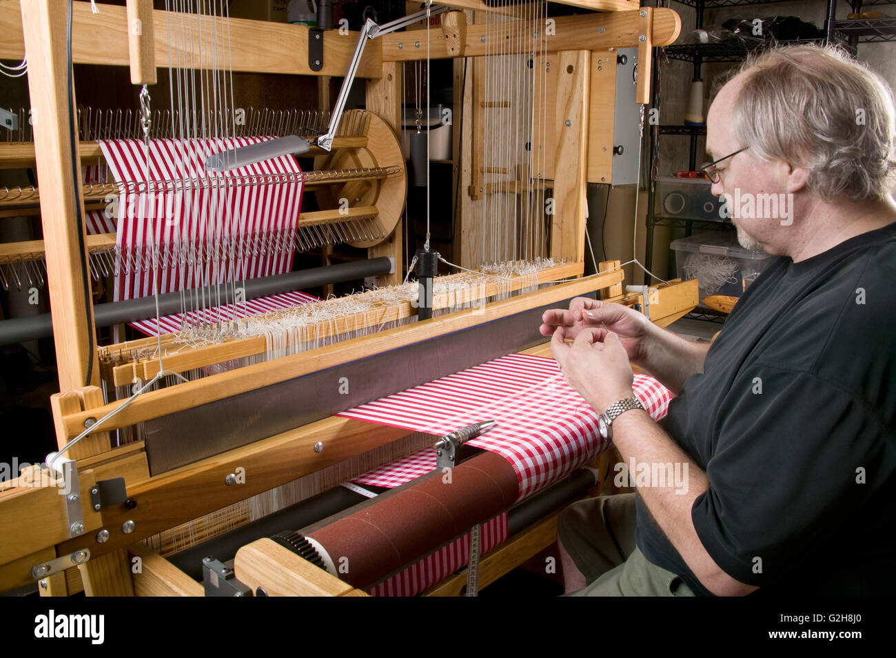 Man fixing broken thread on loom while weaving checkered dish towels on ...