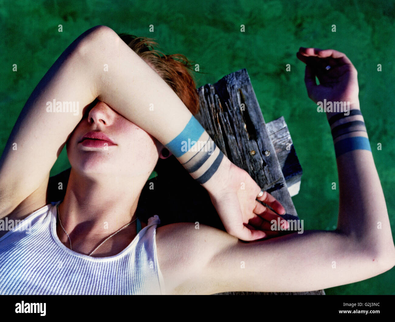 Young Woman With Tattoed Wrists Laying on Dock With Arm Covering Face ...