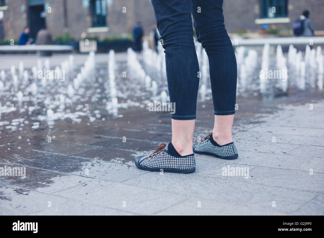 The legs of a young woman as she is standing by a small fountain in the ...