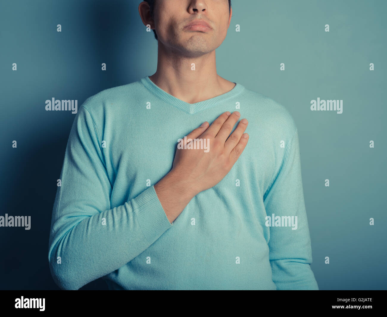 A young man wearing a blue jumper is placing his hand on his chest ...