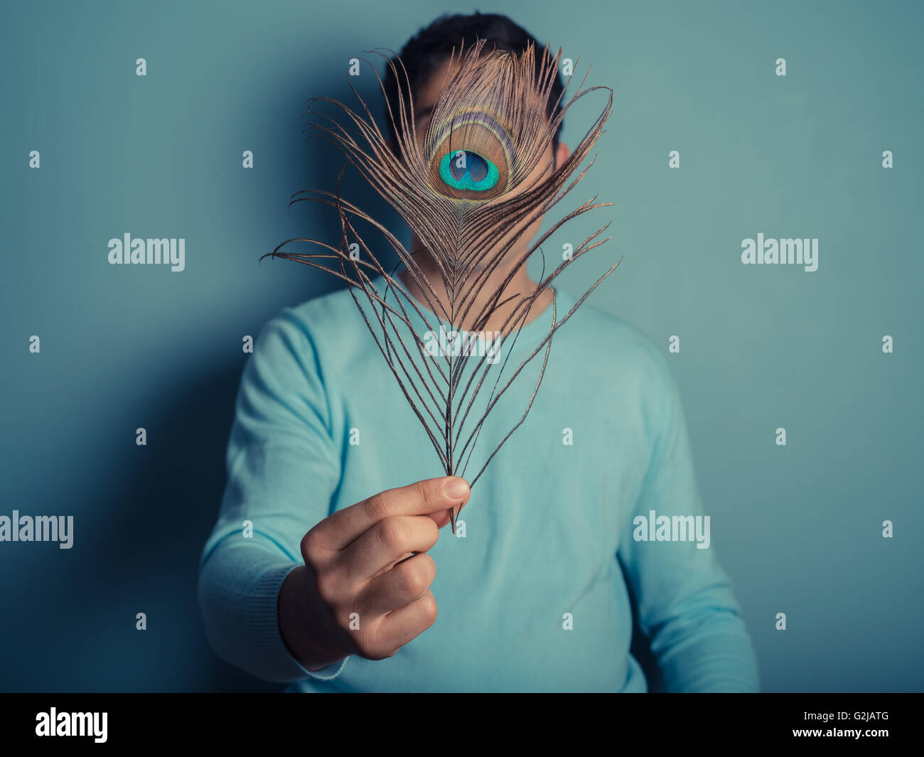 A young man is holding a pretty peacock feather Stock Photo - Alamy