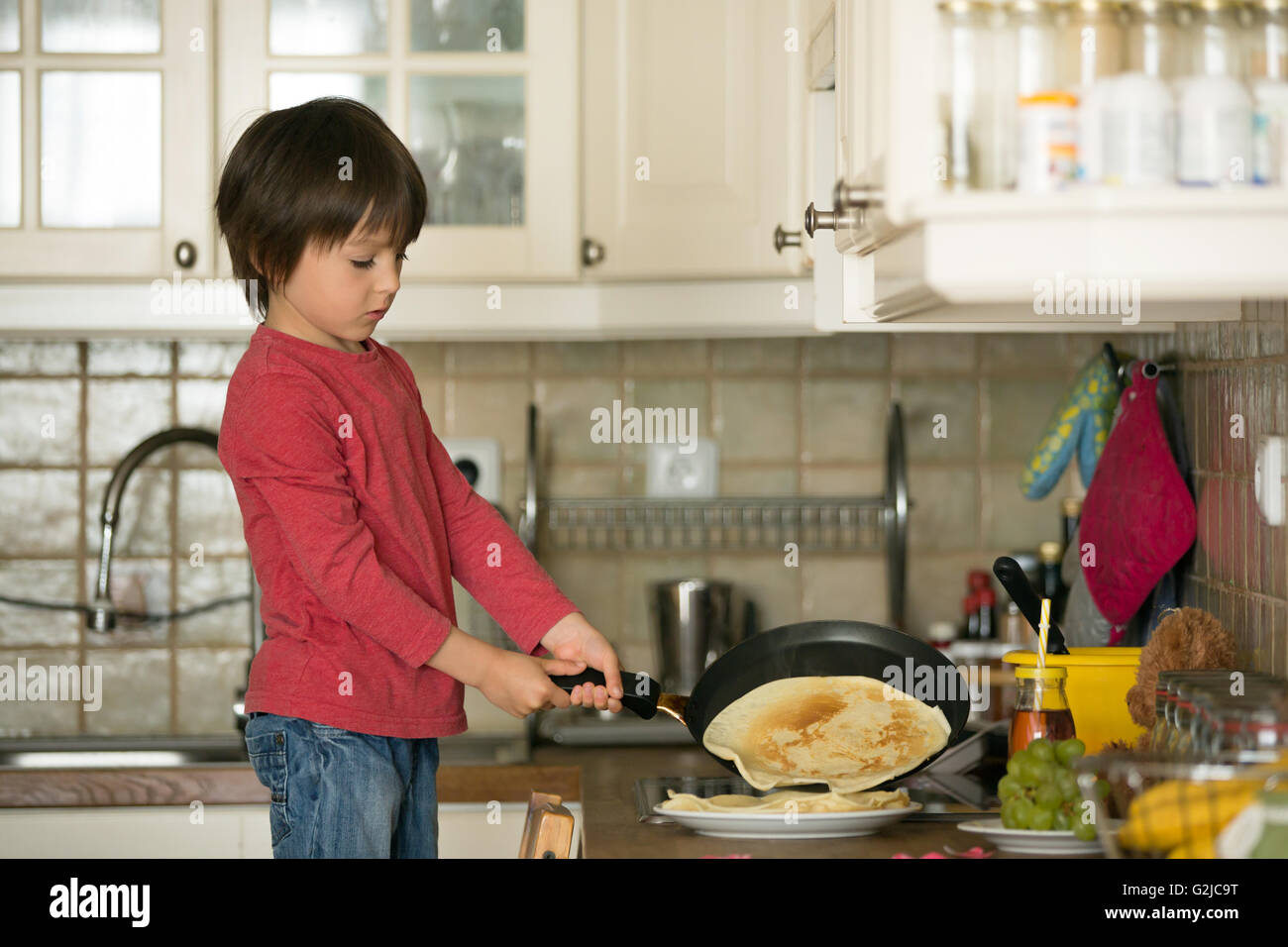 Sweet preschool child, helping his mom in the kitchen, making pancakes ...