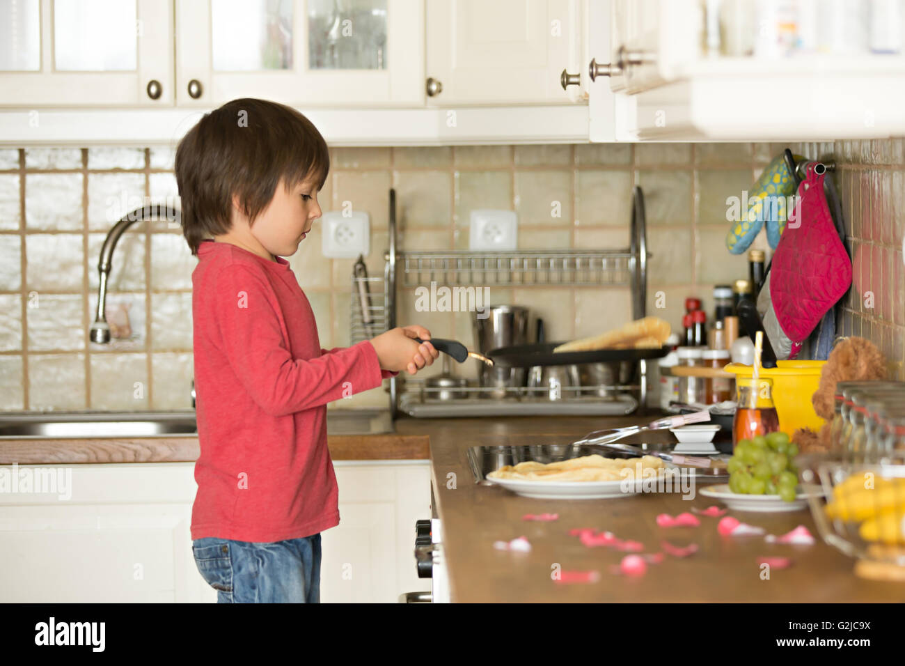 Sweet preschool child, helping his mom in the kitchen, making pancakes ...