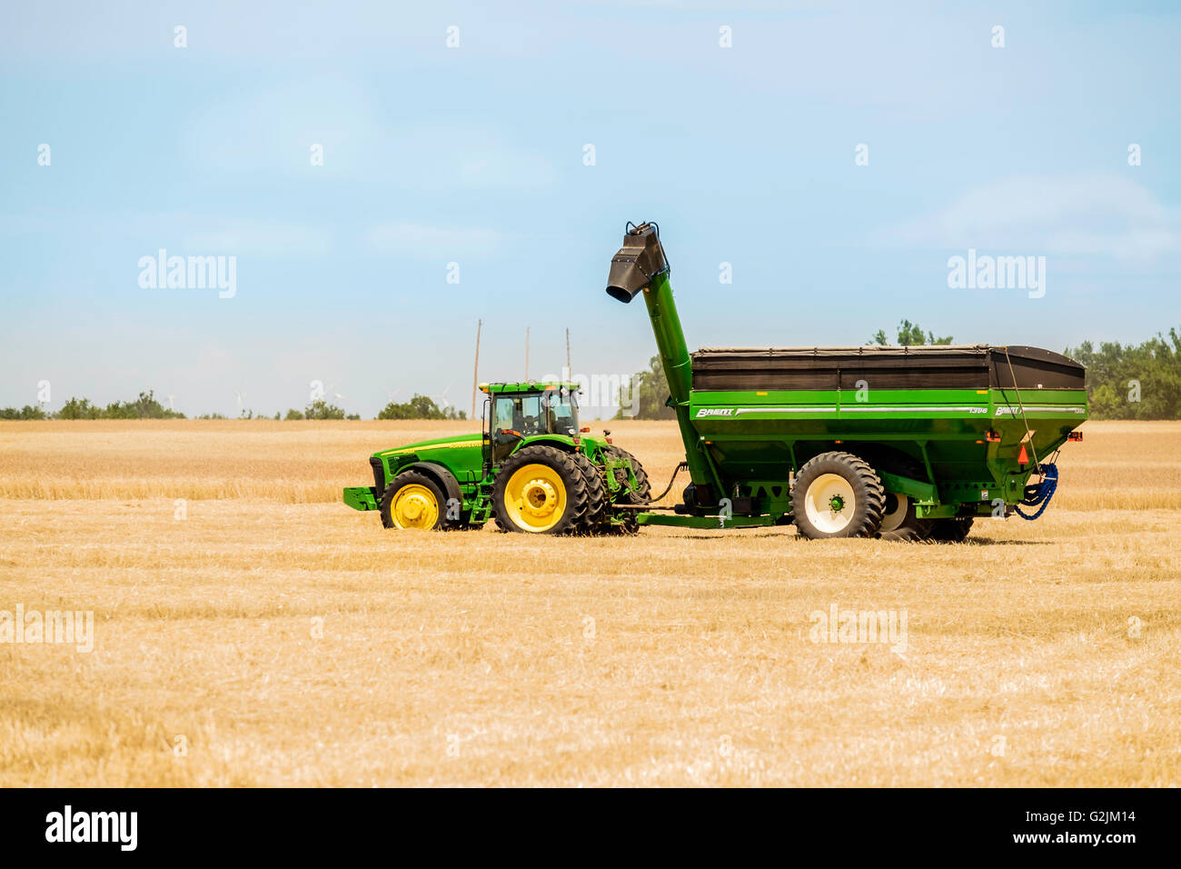 A John Deere tractor pulls a Brent grain cart across a ripe wheat field ...