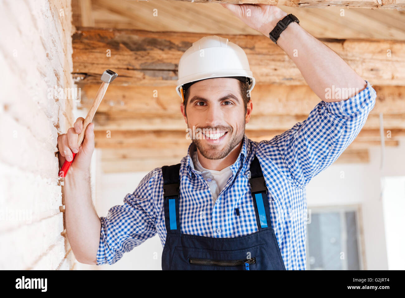 Close-up portrait of cheerful smiling builder using hammer indoors ...