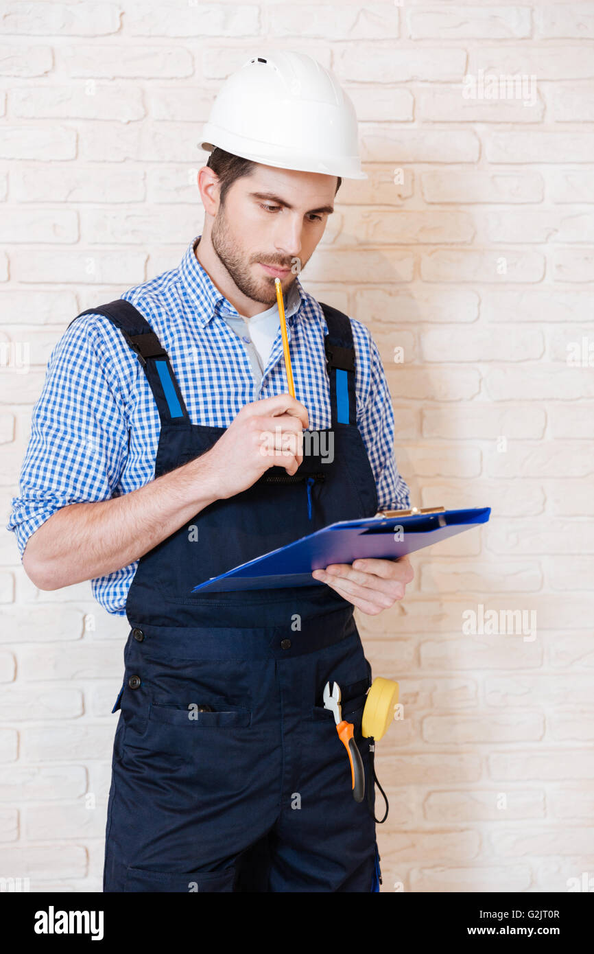 Pensive young construction worker thinking about something using ...