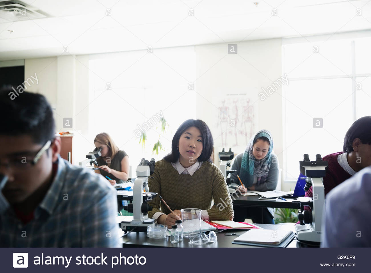 Portrait college student taking notes at microscope in science ...