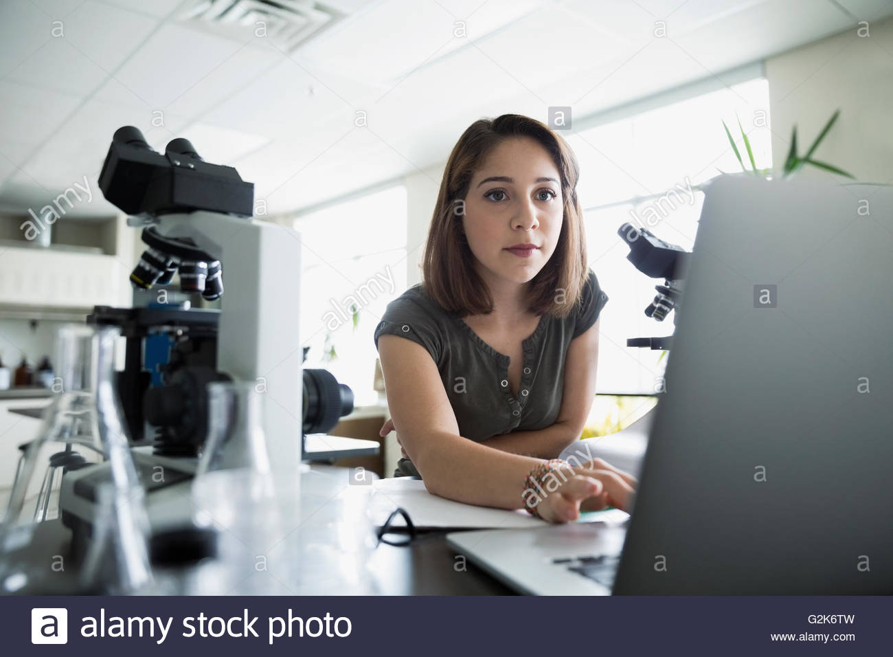 Focused college student using laptop near microscopes in science ...