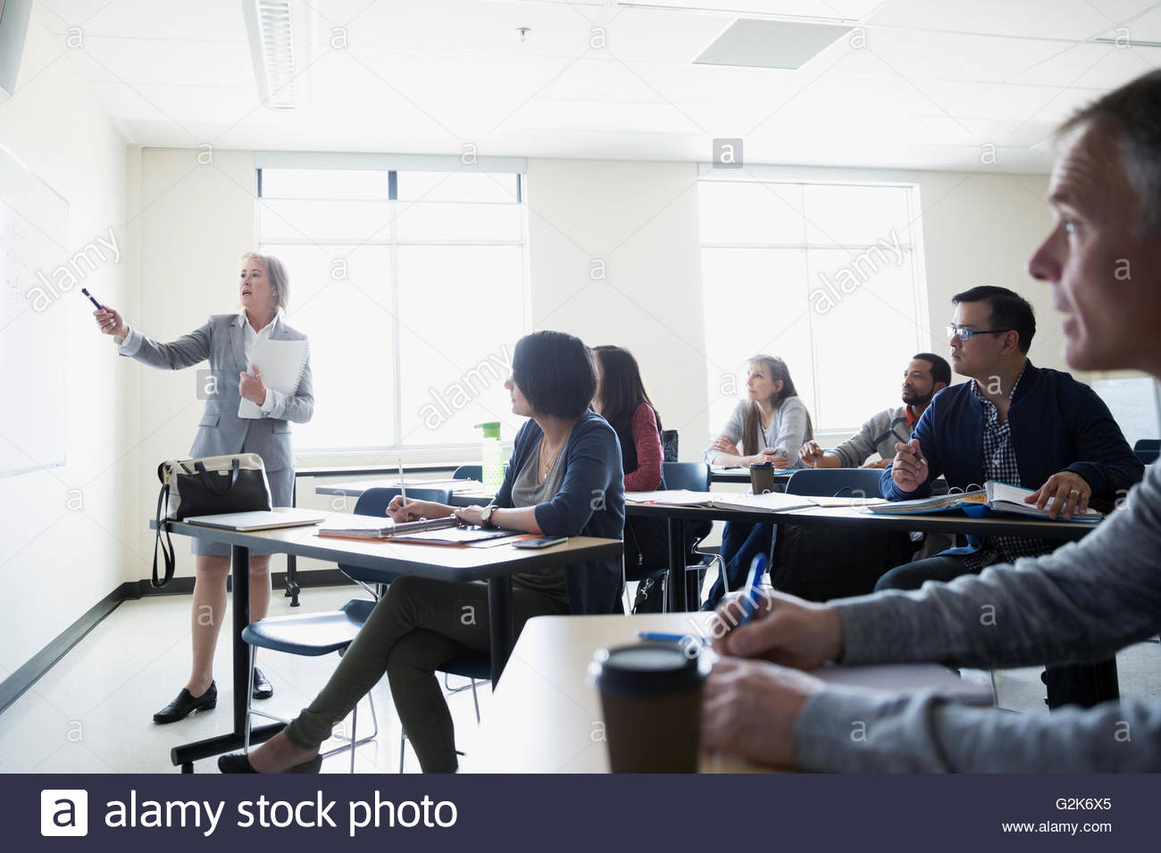 Professor at whiteboard teaching adult education students in classroom ...