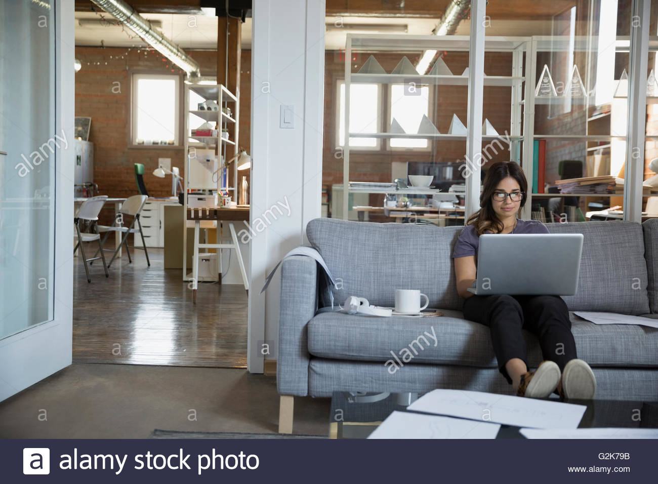 Female designer using laptop on sofa in office Stock Photo - Alamy
