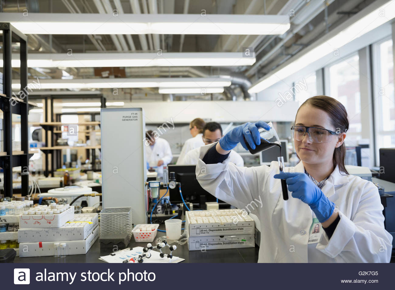 Scientist transferring liquid from beakers to test tube in laboratory ...