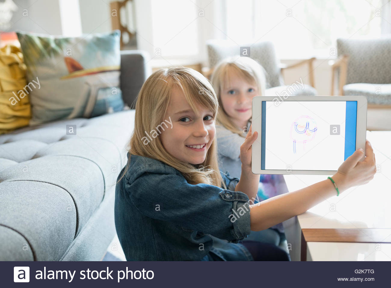 Portrait smiling sisters showing digital tablet drawing in living room ...