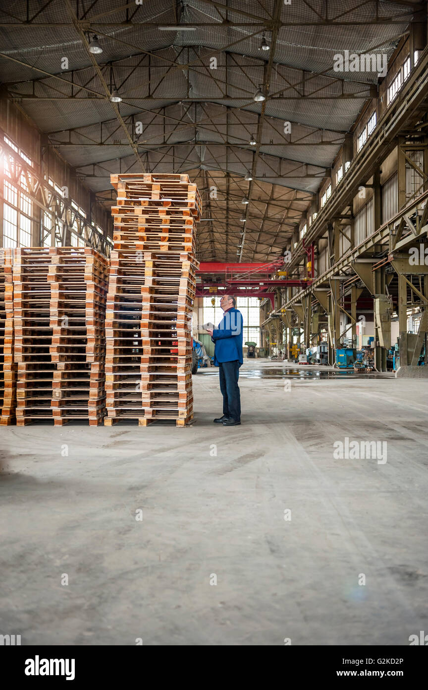 Manager in factory hall looking at stack of pallets Stock Photo - Alamy